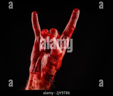 A man's hand covered in blood shows a goat sign on a black background ...