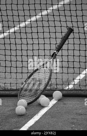 Tennis racket leaning against net with tennis balls on the court ...
