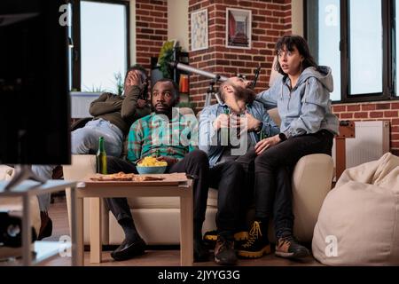 Group of scared friends gathering on sofa and watching horror movie ...