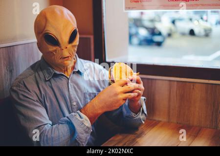 Extraterrestrial ufo alien eating an hamburger at the fast food sitting ...