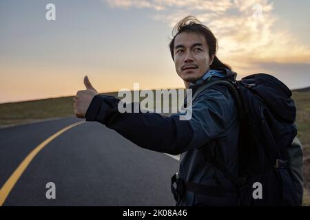 Chinese mid adult man hitchhiking on the road Stock Photo - Alamy