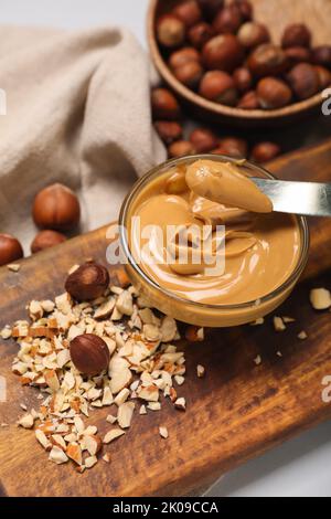 Wooden board with bowl of hazelnut butter on color background, closeup ...