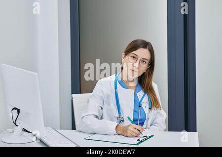 Friendly female general practitioner wearing medical uniform standing ...