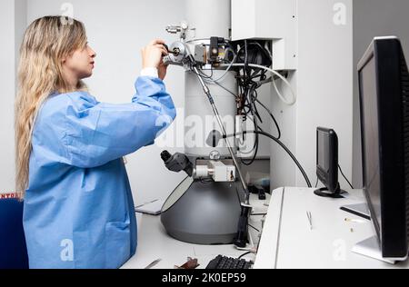 Young female scientist loading a specimen using a sample holder into a ...