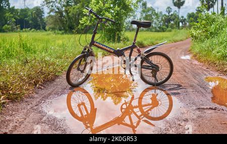 A mountain bicycle and reflection in a puddle of water on a country ...