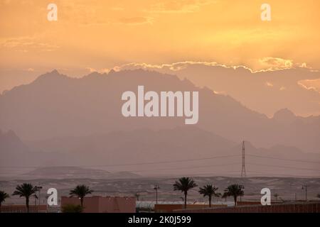 Sunset landscape with remote hotel complex against dark mountain peaks ...