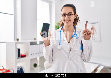 Surprised female doctor, pointing at smartphone app screen, standing ...