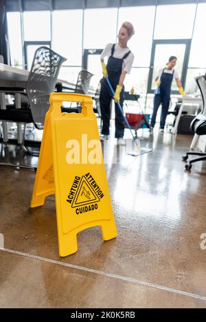 selective focus of caution board near cropped man washing floor with ...