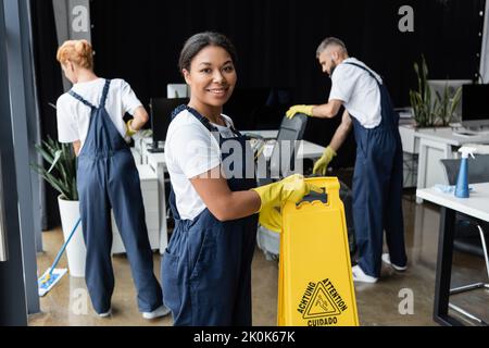 smiling bi-racial woman with detergent looking at camera near ...