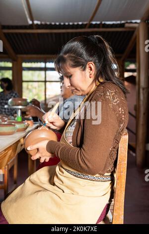 Concentrated Peruvian female artisan in apron painting ceramic bowl ...