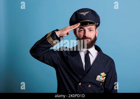 Confident airplane aviator saluting, wearing uniform and hat front view ...