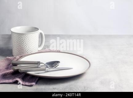 Table setting. White plate, mug, cutlery and napkin on light gray ...