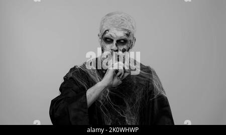 Halloween zombie man presses index finger to lips makes silence gesture ...