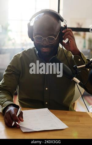 African radio host sitting at desk recording in studio with microphone ...