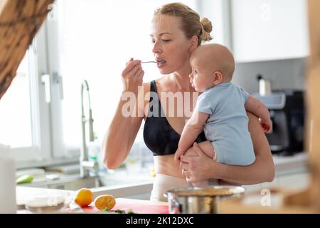 Woman cooking and tasing food while holding four months old baby boy in ...