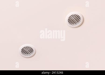 Round air vents with white plastic grate on beige ceiling with copy ...