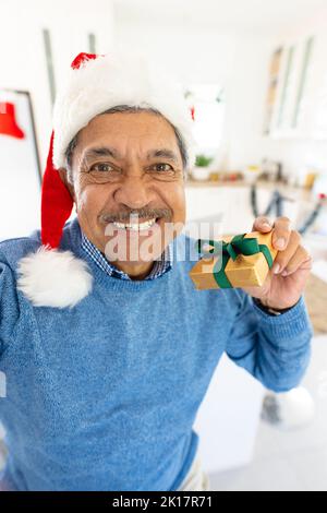 Senior biracial man in santa hat making christmas video call on tablet ...