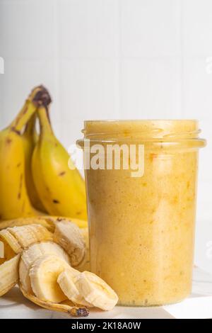 Bananas jam in small glass jar with fresh bananas on white table ...
