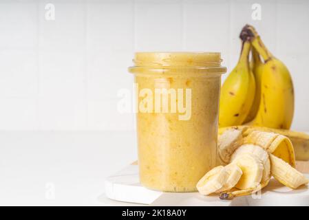 Bananas jam in small glass jar with fresh bananas on white table ...