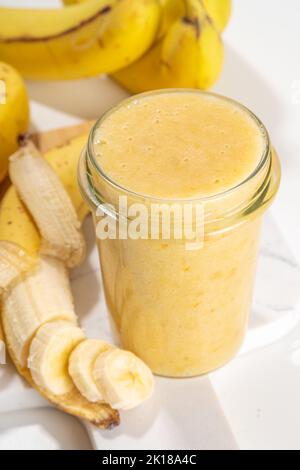 Bananas jam in small glass jar with fresh bananas on white table ...