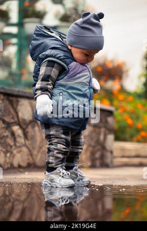 little boy jumps in puddles. Splashes of water fly in different ...