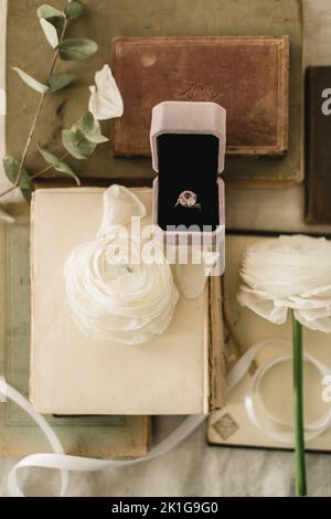A flat lay of open books, artificial rose flowers, and a diamond ring ...