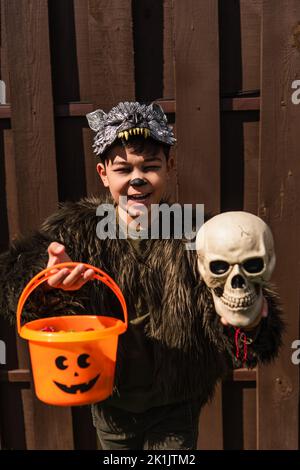 smiling asian boy in werewolf costume looking away while standing with ...