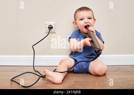 Child boy chewing on the electric wire of a curling iron. Toddler baby ...