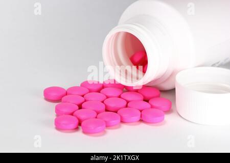 Pink medical pills and tablets spilling out of a drug bottle ...