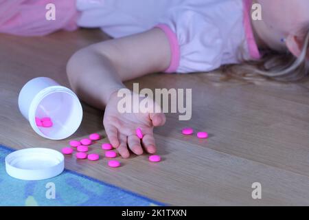 Unconscious little child (girl) with pink pills laying on the floor at ...