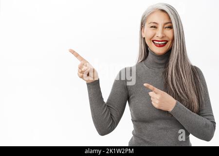 Confident saleswoman pointing left, smiling and looking at camera ...