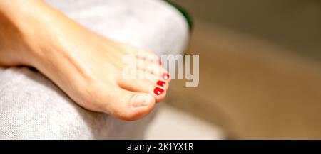 Nail painting process. Red painted fingernails on a female leg in a ...