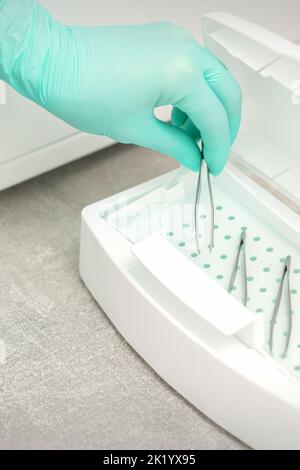 Assistant dentist with tweezers in his hand takes special needle out of ...