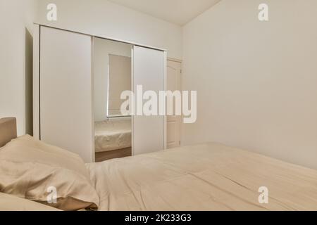 Comfortable bed with blanket and pillows located near closet and ...