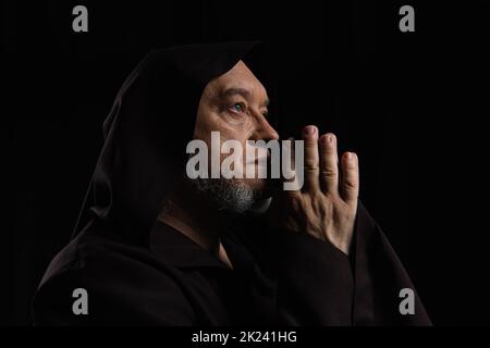 side view of medieval monk praying near inkpot with quills on black ...