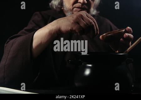 mysterious alchemist adding ingredient into pot while cooking in dark ...