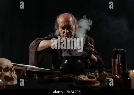 senior alchemist mixing potion in pot while cooking at night isolated ...