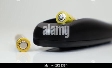 Black remote control with yellow AAA batteries on a white background ...