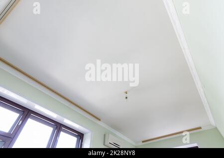 Plastered white ceiling in the room, a temporary light bulb hangs on ...