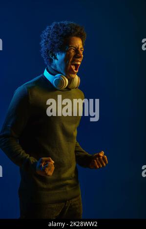 Screaming in headphones. Portrait of young people on light, blue ...