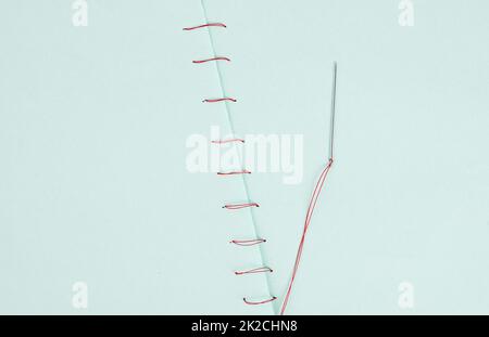 Two pieces of torn paper sewn together with a red string, financial ...