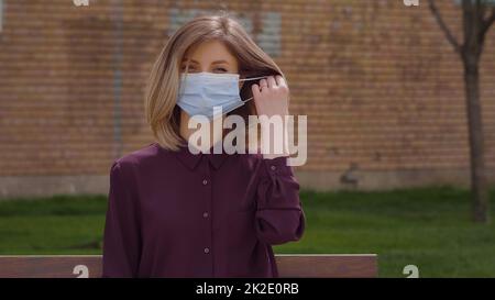 Young woman takes medical mask off her face against blue background ...