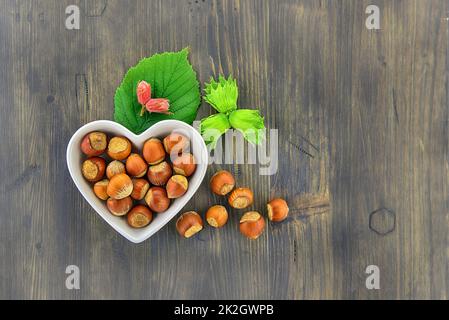 Fresh unshelled hazelnuts in a heart shaped dish with green leaves in ...