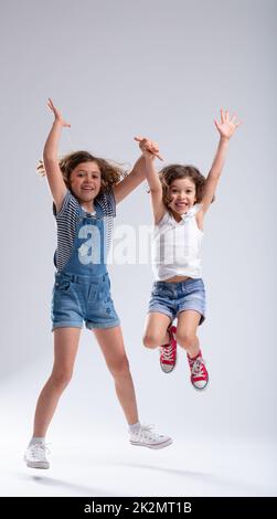 Two exuberant hyperactive young girls jumping for joy with raised arms ...