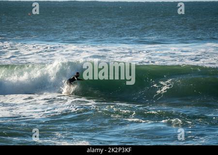 A surfer catching wave and doing turn wearing black wetsuit in morning ...