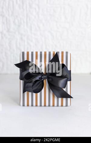 Gift box wrapped in Striped geometric paper with black ribbon bow close ...