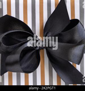 Gift box wrapped in Striped geometric paper with black ribbon bow close ...
