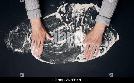 Sifted white wheat flour on a black table and two female hands, top ...