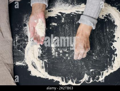 Sifted white wheat flour on a black table and two female hands, top ...
