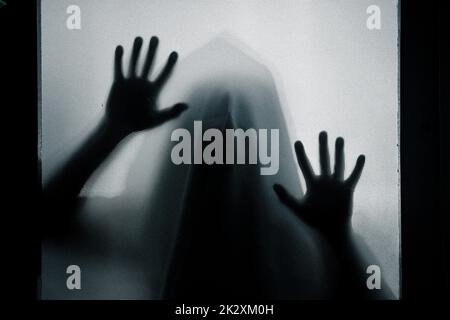Silhouette of creepy ghost behind glass against grey background ...